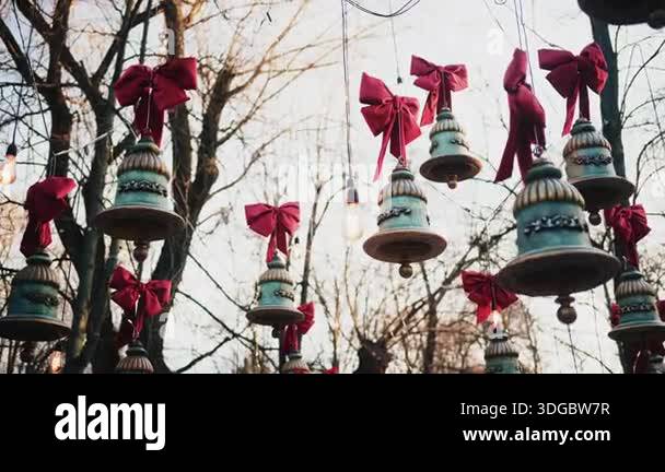 Decorative hanging bells with red bows and warm string lights outdoors ...