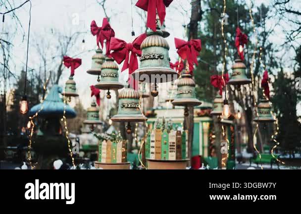 Decorative hanging bells with red bows and warm string lights outdoors ...