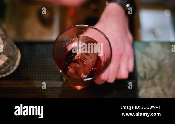 Close up of a bartender stirring a red cocktail with a long bar spoon ...
