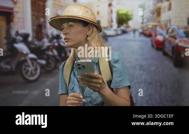 Woman holds smartphone on bustling cobblestone street with parked ...