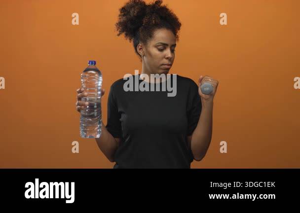 Woman holding water bottle in left hand and 1kg dumbbell in right hand ...