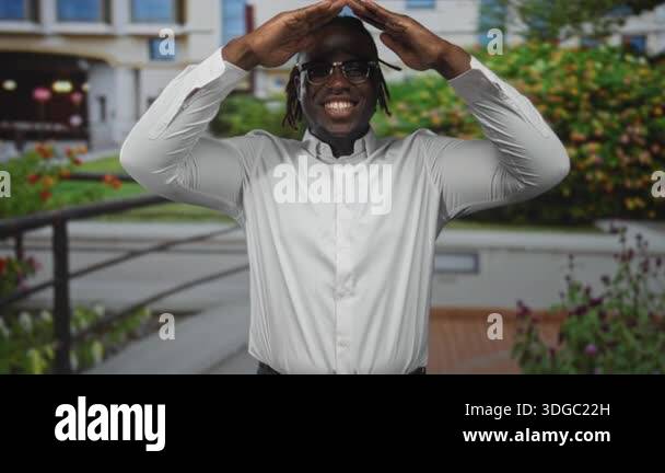 Man smiling and forming a roof with hands in front of building and ...