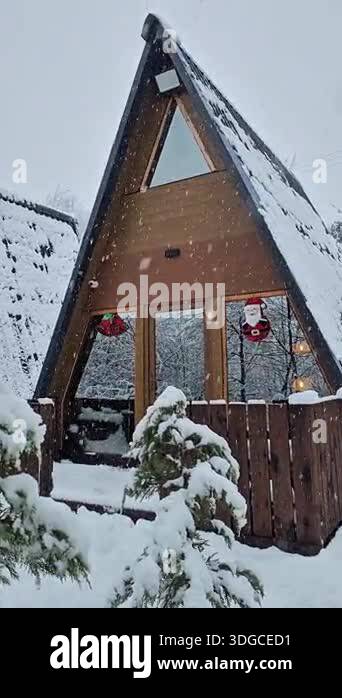 Single wooden A-frame cabin surrounded by snow during snowfall. Snow ...