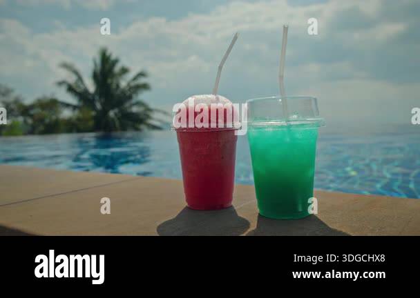 Two frozen tropical drinks in plastic cups on infinity pool edge with ...