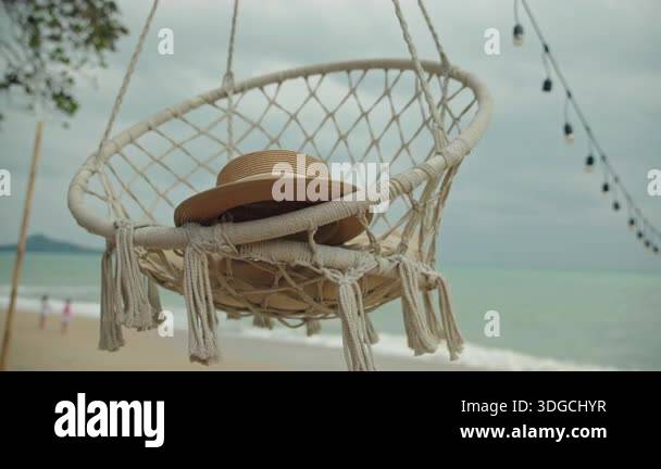 Empty hanging rope swing chair with straw hat on sandy beach in ...