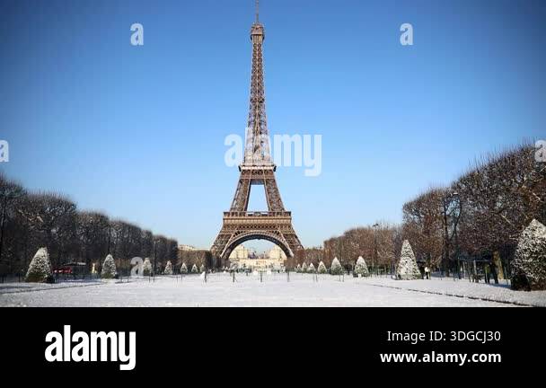 Front view of the Eiffel Tower rising above a snow-covered park in ...