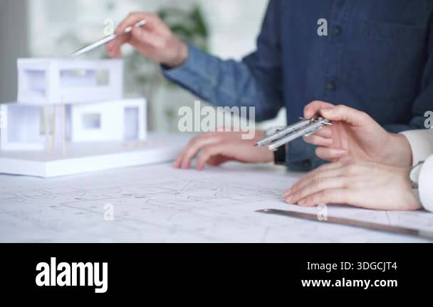 Architects collaborating over blueprints and laptop, pointing to ...