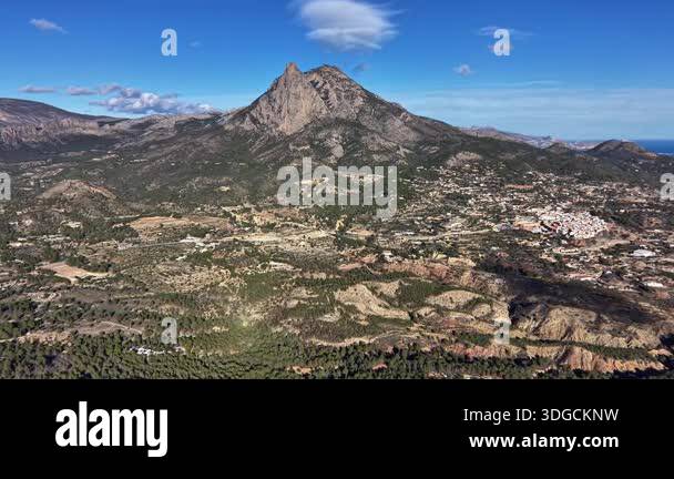 aerial mountain peak overlooking sunlit valley with village and olive ...