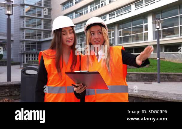 Two young female architects in safety gear discussing building plans ...