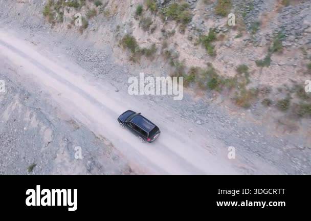 Drone view of black station wagon car driving along dusty dirt road in ...