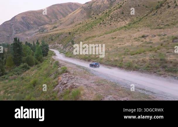 Drone view of black station wagon car driving along dusty dirt road in ...