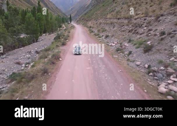 Drone view of black station wagon car driving along dusty dirt road in ...