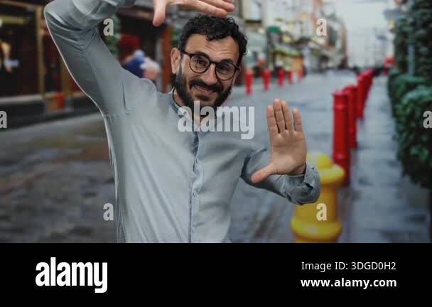 Hispanic man with beard and glasses frames hands playfully on busy ...