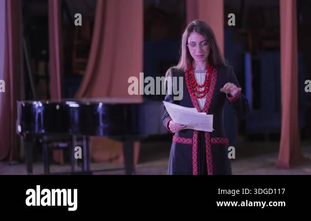 A woman in traditional Ukrainian clothing conducts an orchestra or ...