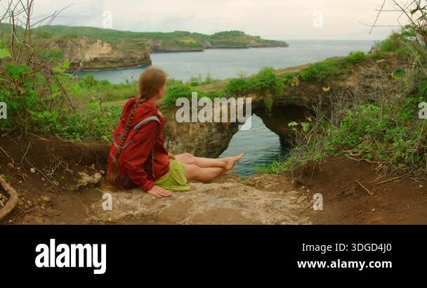 Tourist woman sits on cliff edge overlooking famous Broken Beach ...