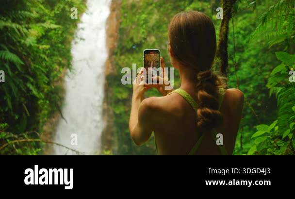 Tourist filming tall Costa Rica waterfall surrounded by lush rainforest ...