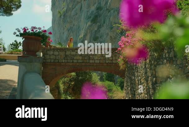 Tourist exploring on stone bridge with flowers overlooking cliffs in ...
