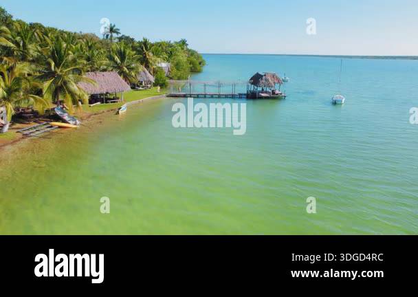 Pier with thatched roof huts extending into calm green waters of ...