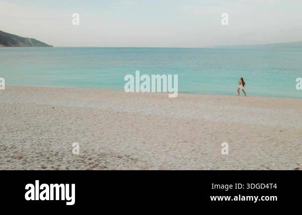 Happy woman jogging along a quiet pebble beach beside calm turquoise ...
