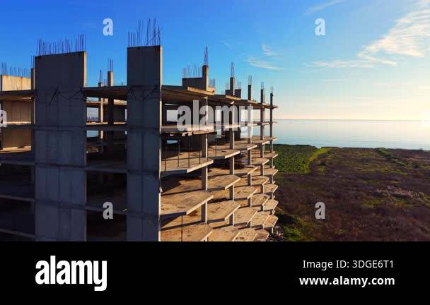 Unfinished multi-story building near shoreline with visible slabs ...