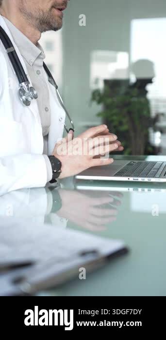 Doctor wearing a lab coat and stethoscope, typing on a modern laptop at ...