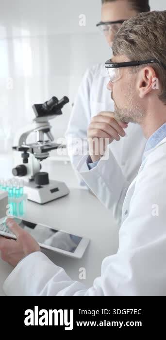 A male scientist takes notes on a tablet while his female colleague ...