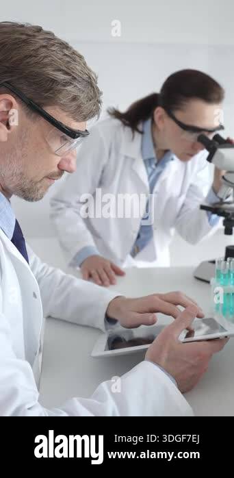 A male scientist takes notes on a tablet while his female colleague ...