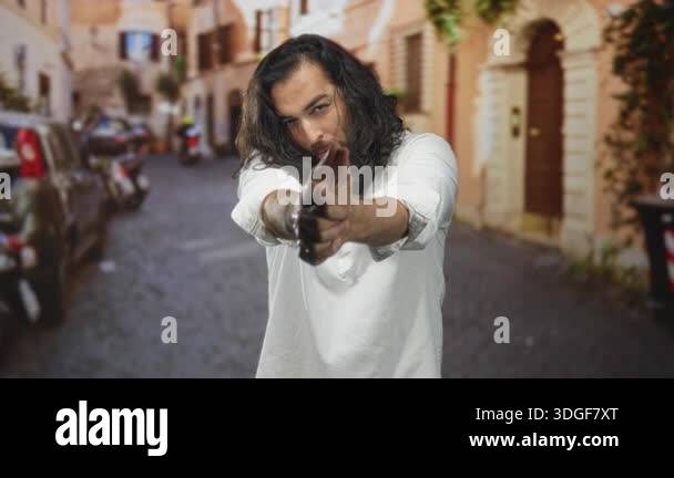 Man pointing finger like gun toward camera on old town street with long ...
