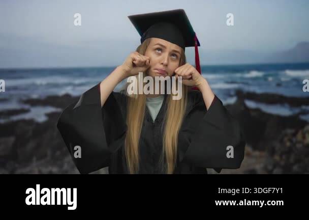 Young woman in graduation uniform playfully crying at the beach, with ...