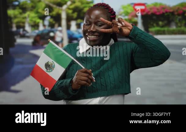 Woman smiling and holding a mexican flag while making a peace sign on a ...