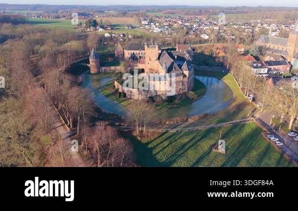 Aerial view of red brick medieval castle with moat and towers, set in a ...