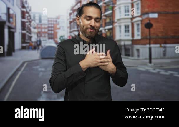 Young arab hispanic man holding hands over chest on urban street with ...