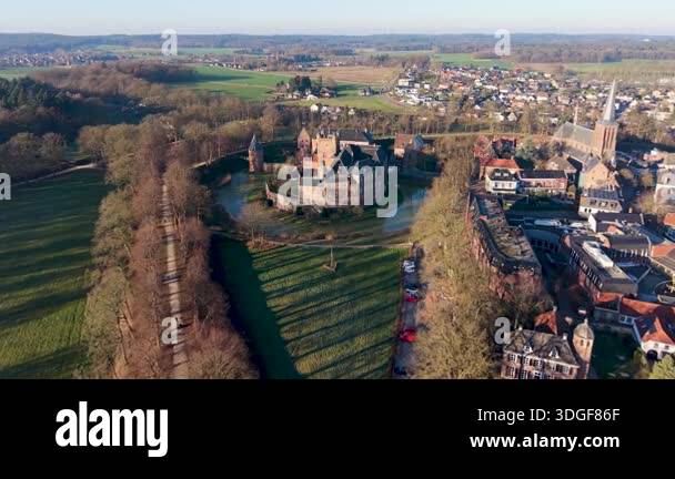 A medieval castle with a wide moat stands beside a tall steepled church ...