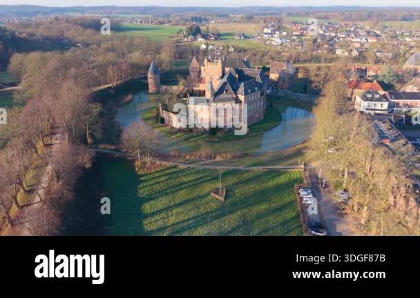 A medieval castle with a wide moat stands beside a tall steepled church ...