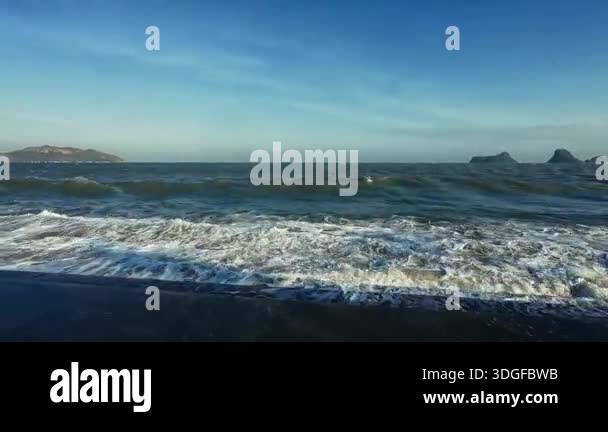 Powerful ocean waves crash against dark concrete shore with distant ...