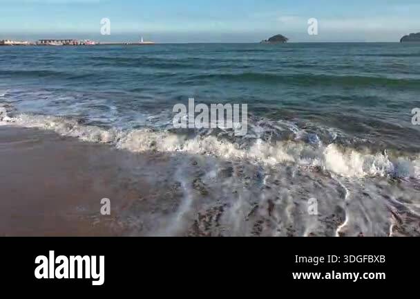 Gentle ocean waves roll onto sandy shore with distant islands ...