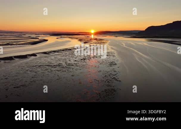 Sunrise at low tide, sun reflecting off black volcanic sand. High ...