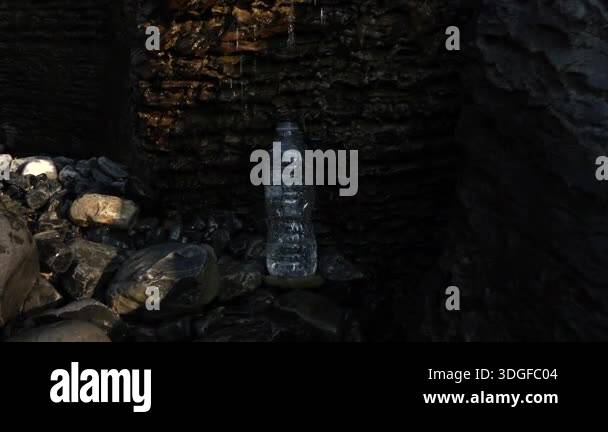 Fresh water dripping into a plastic bottle surrounded by rocks and ...
