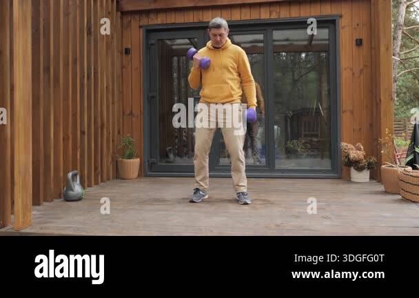 Man Exercising With Dumbbells on Wooden Terrace Near Modern House ...