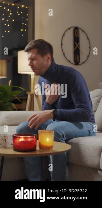 Sick man sitting on sofa at home and holding chest, coughing and ...