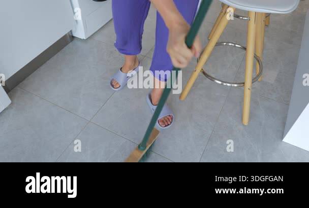 Woman sweeping kitchen floor with broom in modern home interior ...