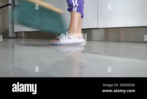 Woman sweeping kitchen floor with broom in modern home interior ...
