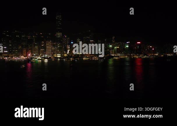 Dark water mirrors neon as ferries cross bay and building tower windows ...