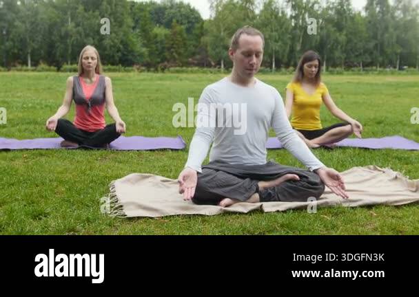 Group of sportsmen performs breathing exercise outdoors in a green park ...