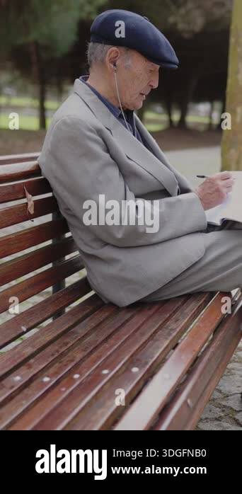 Senior man taking notes in his notebook while sitting on a bench in a ...