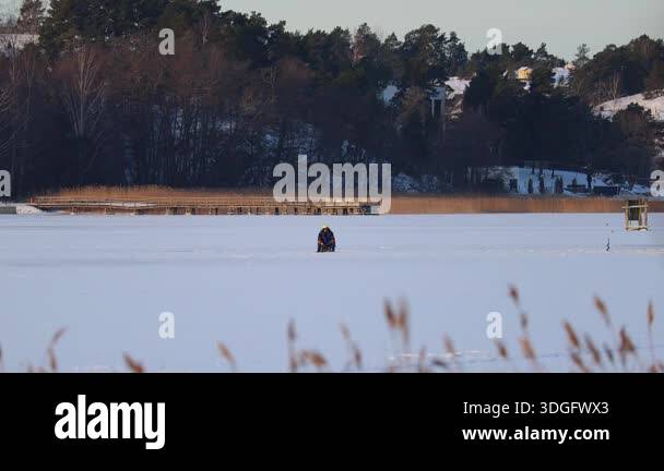 4K video of a fisherman ice fishing on a frozen winter lake. The scene ...