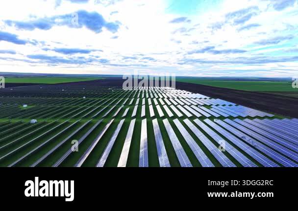Aerial view shows rows of solar panels reflecting sunlight across green ...