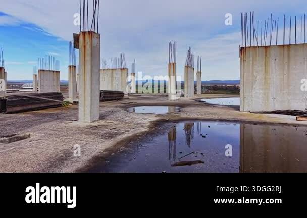 Water pools reflect the sky at an unfinished construction site. Columns ...
