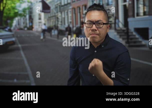Man clenches fist and grimaces on a city street near buildings, wearing ...