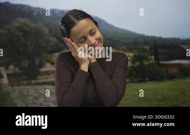 Woman in a park mimicking sleep with hands clasped under cheek, smiling ...